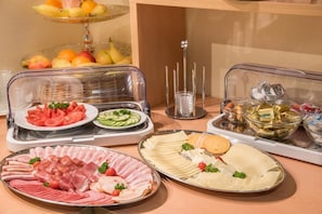 Buffet com diversas opções de comida, incluindo frutas, queijos e carnes.