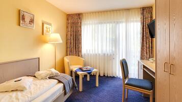 Quarto de hotel com cama, escrivaninha, cadeira, abajur, televisão e cortinas.