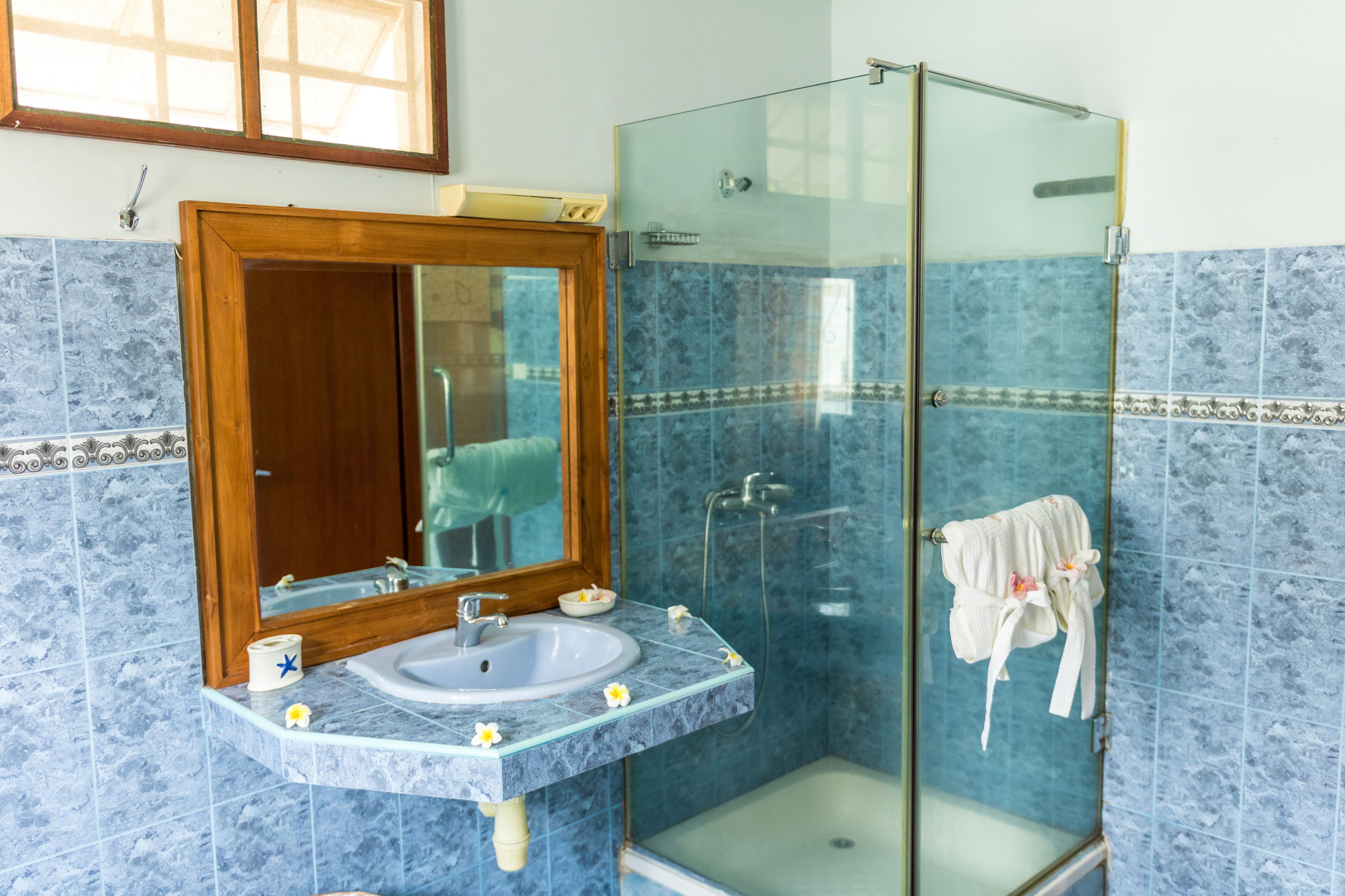 Um banheiro com box de vidro, pia com espelho e paredes com azulejos azuis.