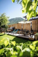 Um deck de madeira com mobiliário externo, incluindo cadeiras e uma mesa, com montanhas ao fundo.