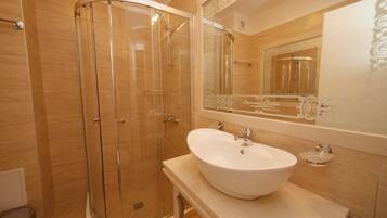 Um banheiro moderno com chuveiro em box de vidro, pia branca e um espelho grande.