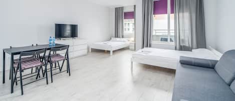Quarto de hotel moderno com cama, sofá, escrivaninha e cadeiras, e uma televisão.