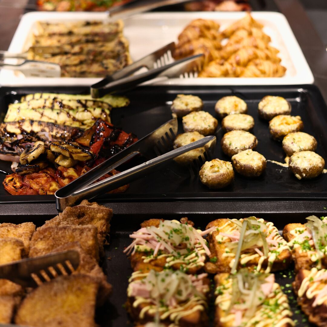Buffet variado com diversos pratos, incluindo legumes grelhados, almôndegas e pão.