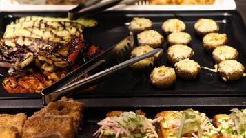 Buffet variado com diversos pratos, incluindo legumes grelhados, almôndegas e pão.