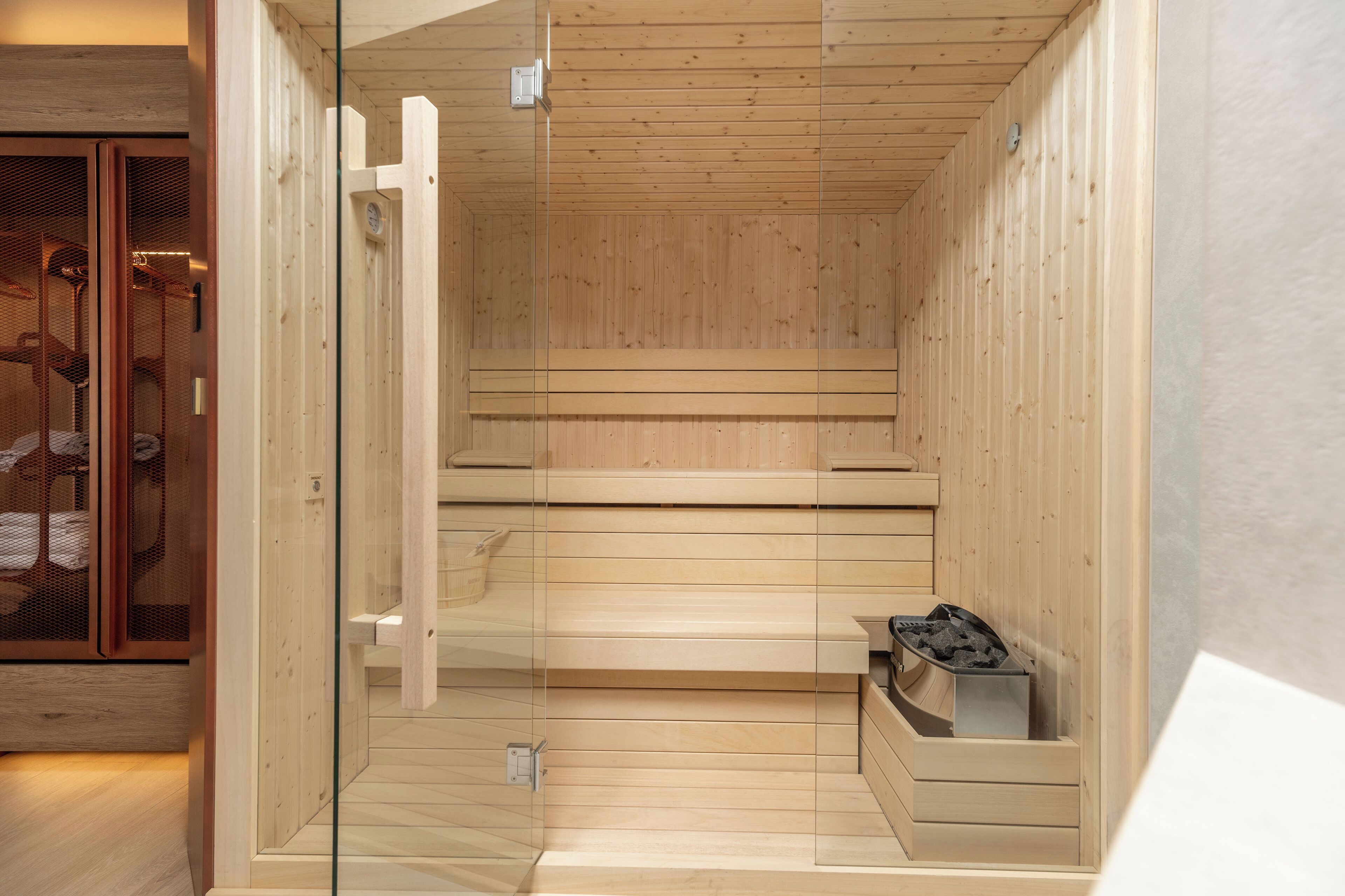 Uma sauna com paredes de madeira e porta de vidro, um banco e uma pequena prateleira com objetos.