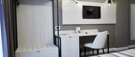 Quarto de hotel moderno com uma cama, uma escrivaninha, uma cadeira e uma televisão fixada na parede.