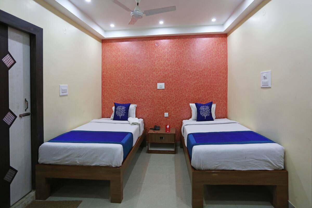 Quarto com duas camas de madeira, cada uma com colcha azul e roupa de cama branca, um ventilador de teto e uma parede com padrão vermelho.
