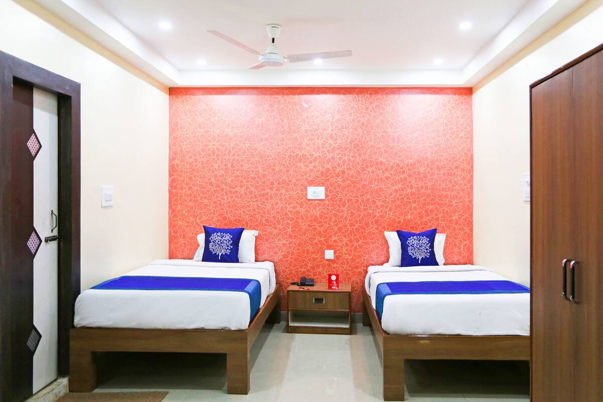 Quarto de hotel com duas camas de solteiro, um ventilador de teto e uma parede com padrão vermelho.