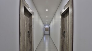 Um corredor comprido e estreito com portas de madeira em ambos os lados e chão de azulejos.