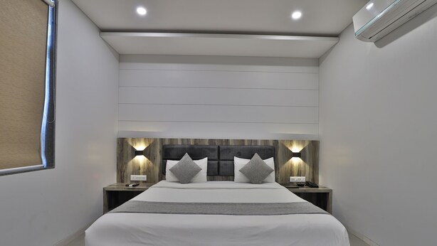 Quarto de hotel moderno com uma cama grande, duas mesas de cabeceira com abajures, uma cabeceira de madeira e um ar condicionado fixado na parede.