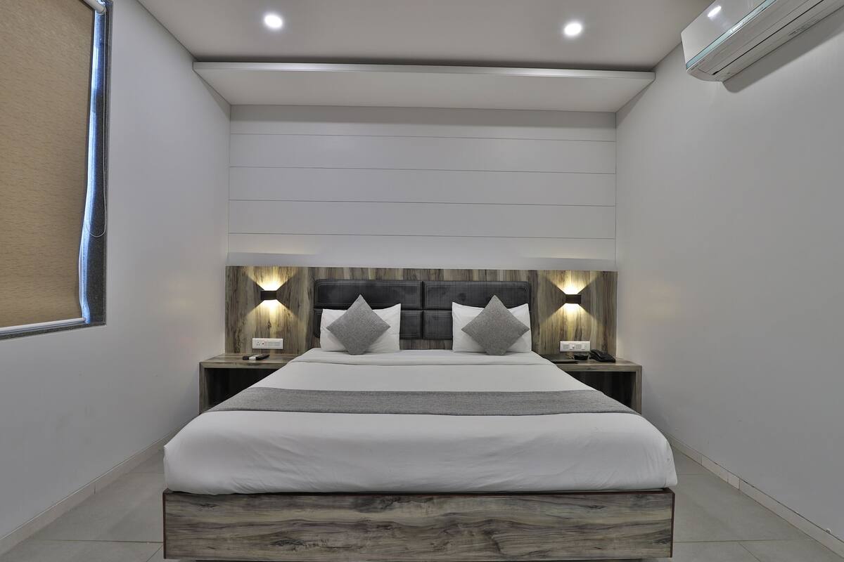 Quarto de hotel moderno com uma cama grande, duas mesas de cabeceira com abajures, uma cabeceira de madeira e um ar condicionado fixado na parede.