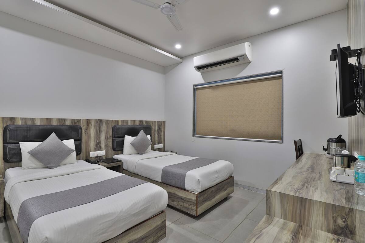 Quarto de hotel com duas camas, uma escrivaninha com uma garrafa de água, uma televisão e um ar condicionado.