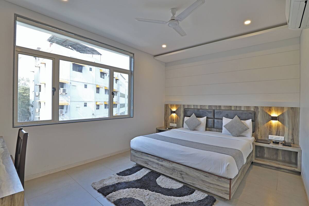 Quarto moderno com uma cama grande, um ventilador de teto e vista para edifícios lá fora.