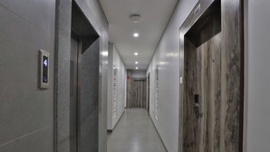 Um corredor moderno com um mostrador de elevador digital, um alarme de incêndio e uma porta de madeira.