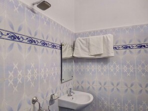 Casa de banho com azulejos estampados, uma pia, um espelho e um porta-toalhas.