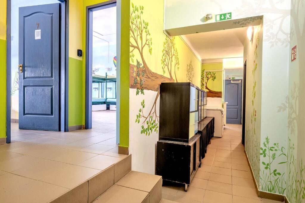 Corredor de hotel com uma porta azul, escadaria e parede com painéis de árvores.