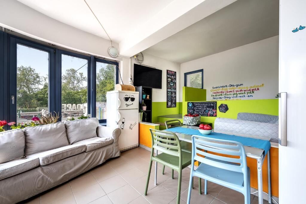 Quarto moderno com sofá, mesa de jantar e cadeiras, televisão e parede decorada com diversos enfeites.
