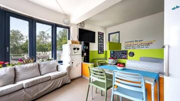 Quarto moderno com sofá, mesa de jantar e cadeiras, televisão e parede decorada com diversos enfeites.