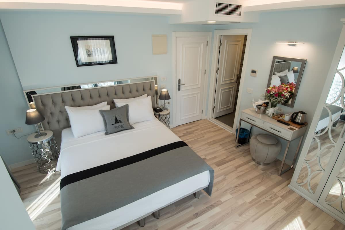 Quarto de hotel moderno com uma cama grande, mesas de cabeceira, uma escrivaninha e um espelho.