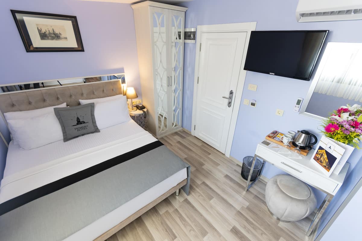 Quarto com cama, mesa de cabeceira, guarda-roupa, televisão e escrivaninha com cadeira.