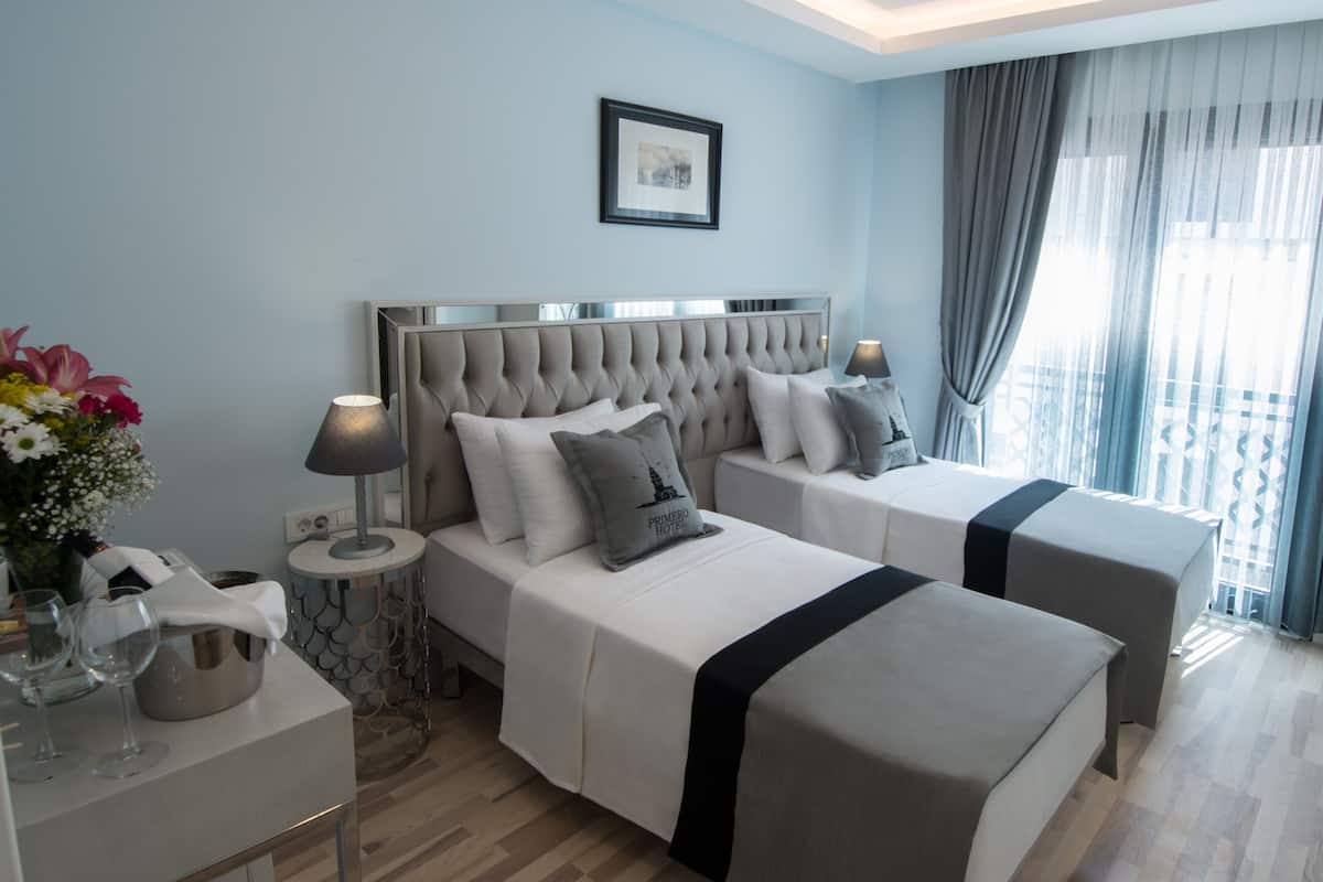 Quarto de hotel com duas camas, uma mesa de cabeceira com abajur, um vaso com flores e um quadro pendurado na parede.
