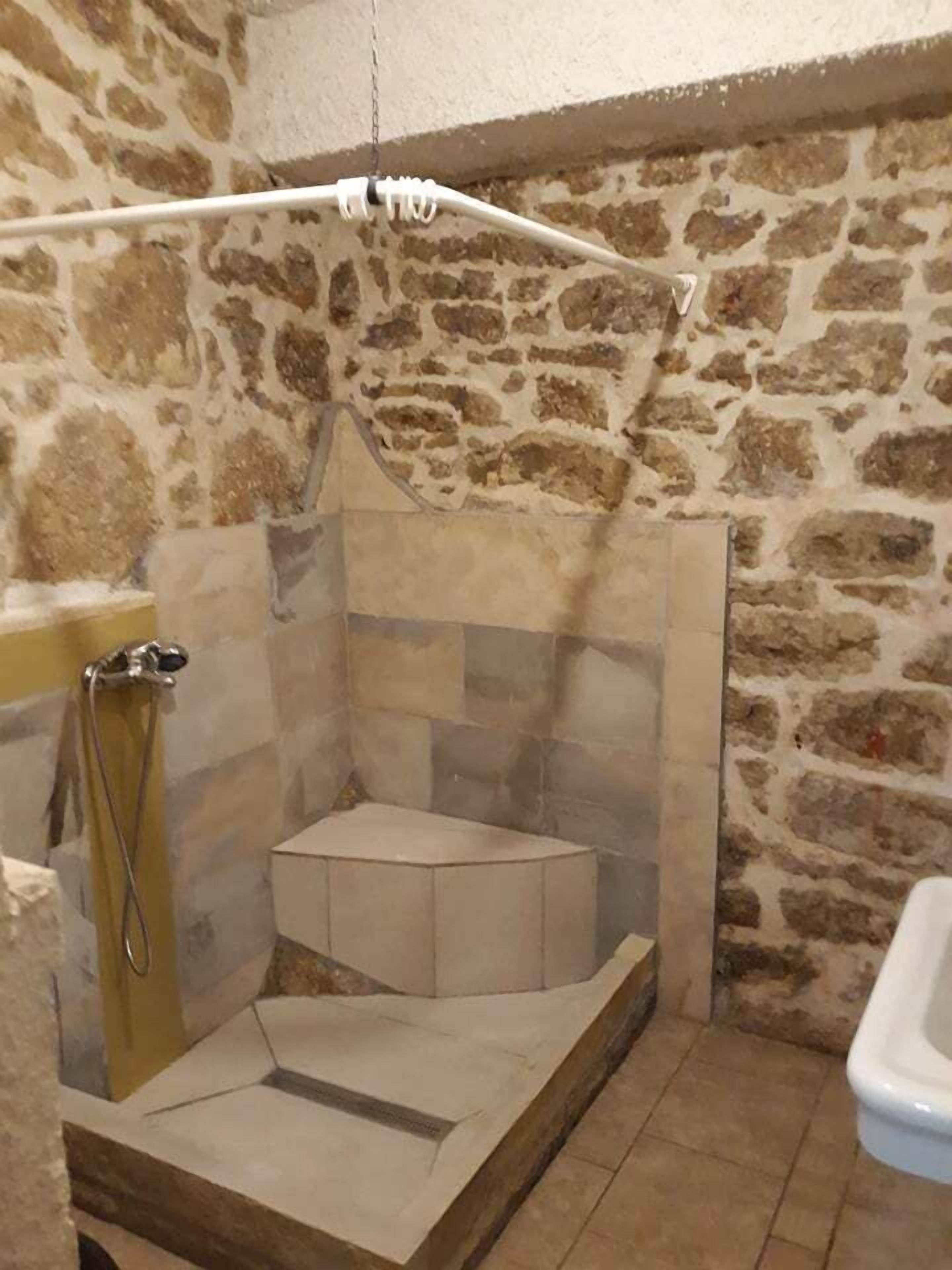 Casa de banho com paredes de pedra, chuveiro, banheira e sanita.