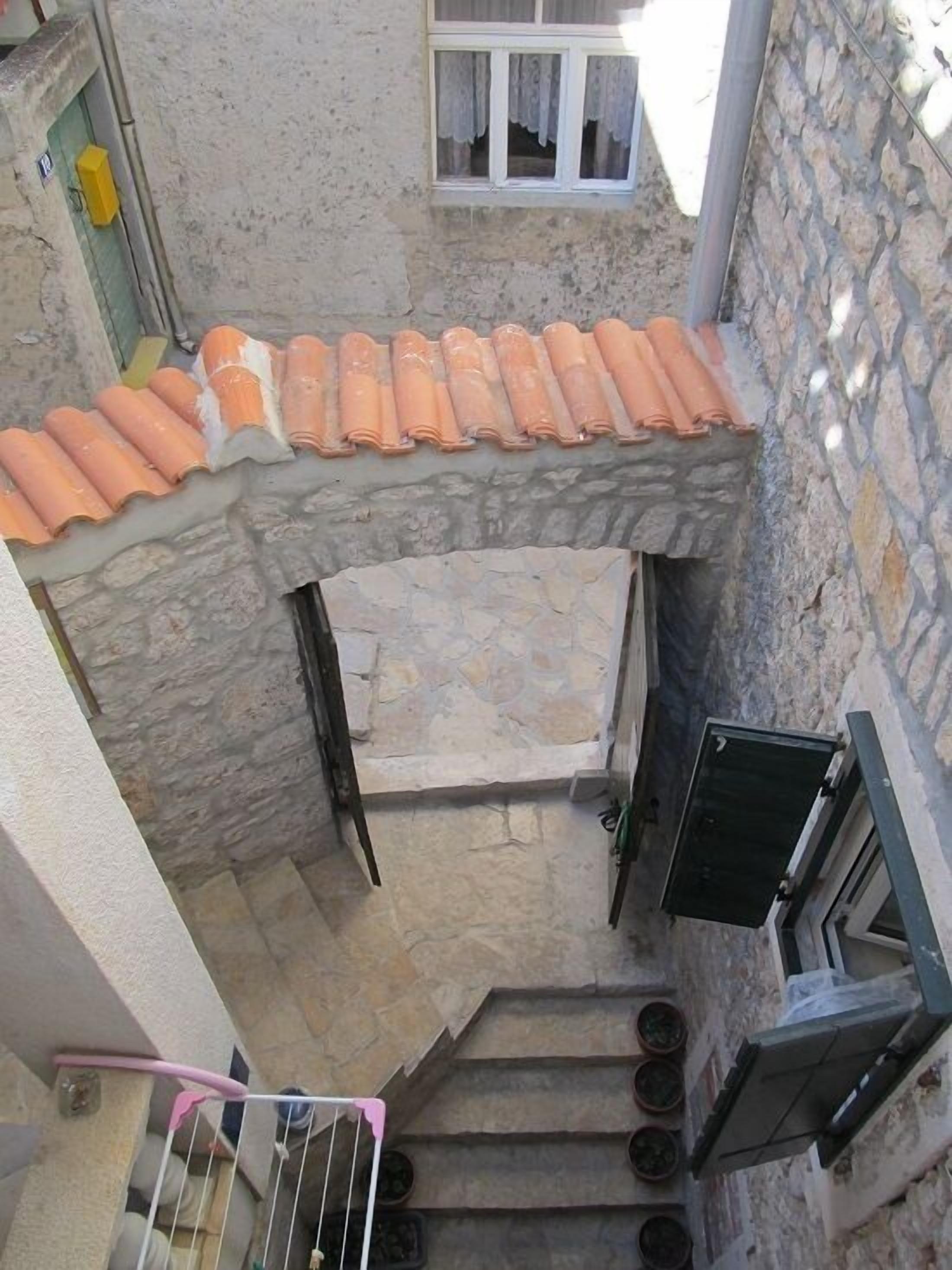 Uma escadaria estreita com paredes de pedra, telhado em azulejos e uma pequena janela.