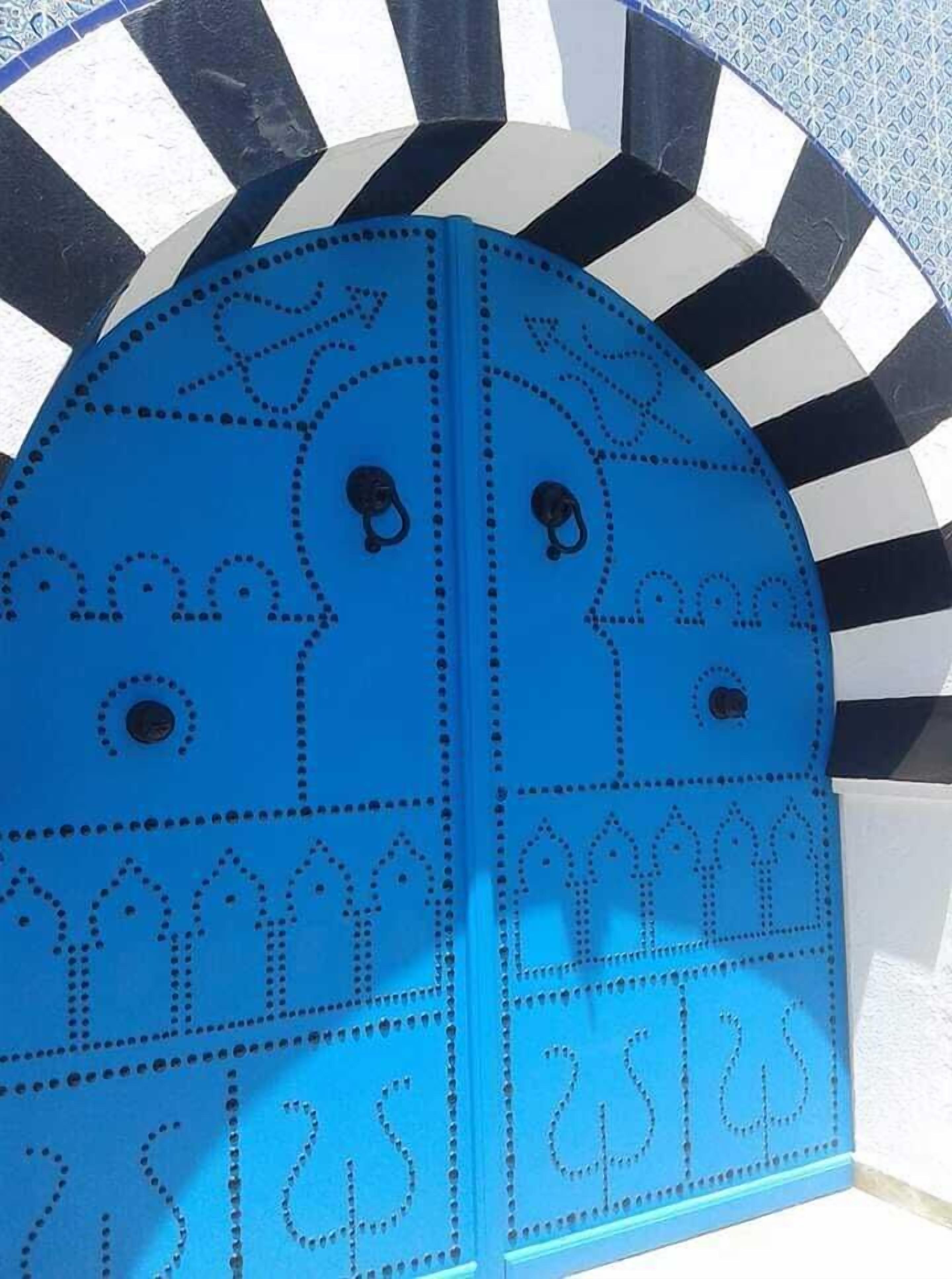 Uma porta azul com padrões elaborados e duas maçanetas circulares.