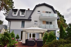 Uma casa de dois andares com varanda, um pátio com mobiliário de exterior e um jardim.