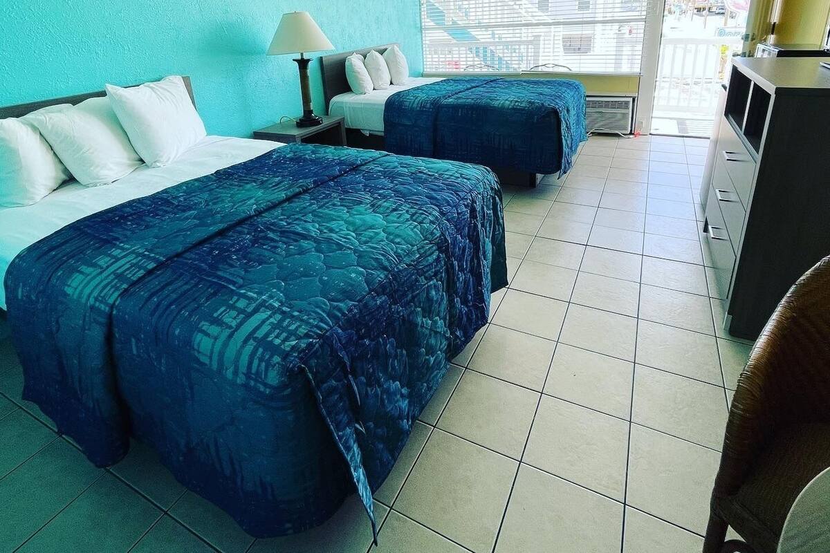 Quarto de hotel com duas camas, televisão e janela com persianas.