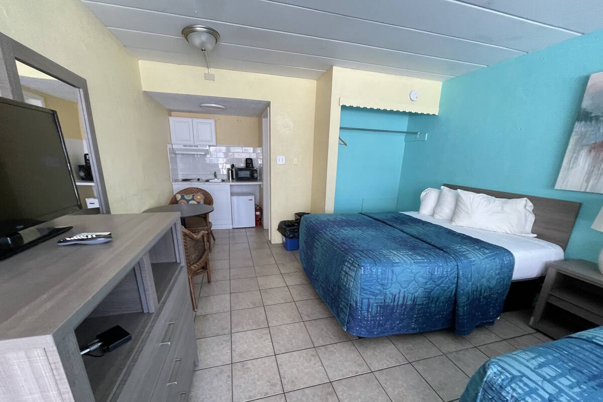 Quarto de hotel compacto com uma cama, uma escrivaninha com televisão, uma cozinha compacta e um banheiro.