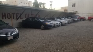 Fila de carros estacionados numa área de estacionamento com calçamento, com um edifício ao fundo com a inscrição 'HOTEL OUTSIDE'.