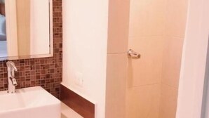 Casa de banho com lavatório branco, espelho e chuveiro.