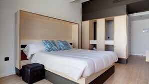 Quarto moderno com cama grande, armário embutido e um pequeno espaço de estar.