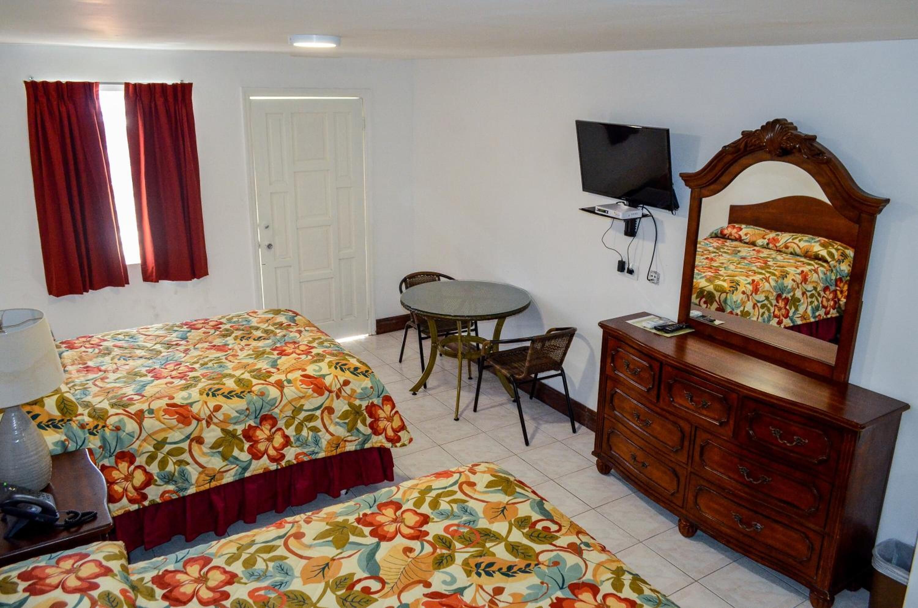 Quarto com duas camas, cômoda, televisão e mesa de jantar.