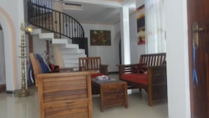 Uma sala de estar ampla com um conjunto de sofá de madeira, uma mesa de centro e uma escada que leva a um andar superior.