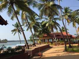 Um resort à beira-mar com palmeiras, piscina e um edifício com telhado vermelho.