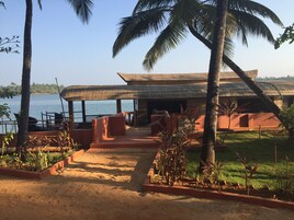Um resort na praia com uma construção de colmo, um caminho de areia e vista para o mar.