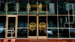 Entrada de um hotel com uma placa grande indicando "HOTEL WEST SHINE" e estrelas decorativas acima da entrada.