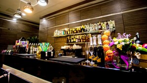 Uma área de bar com diversas garrafas de bebidas, uma máquina de café e uma seleção de frutas e flores.