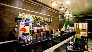 Uma área de bar com um letreiro da Red Bull, prateleiras com diversas garrafas e um letreiro de cafeteria.