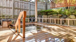 Um deck de madeira com uma banheira de hidromassagem, cercado por um muro de madeira e uma parede de pedra.