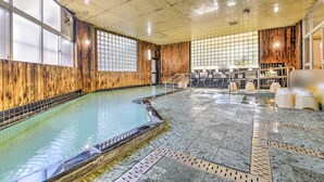 Piscina interna com lambris de madeira e paredes revestidas de azulejos, cercada por áreas de estar e piso cerâmico.