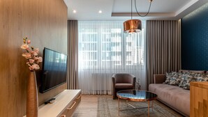 Uma sala de estar moderna com televisão de tela plana, um vaso com flores, uma poltrona marrom, uma mesa de centro redonda e um sofá com almofadas estampadas.