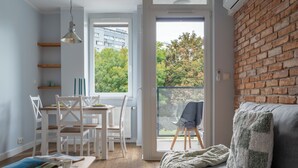 Uma sala de estar moderna com sofá, mesa de jantar com cadeiras, janela com vista para árvores e parede de tijolos.