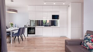 Cozinha moderna com armários brancos, área de jantar com mesa e cadeiras, e sala de estar com sofá.