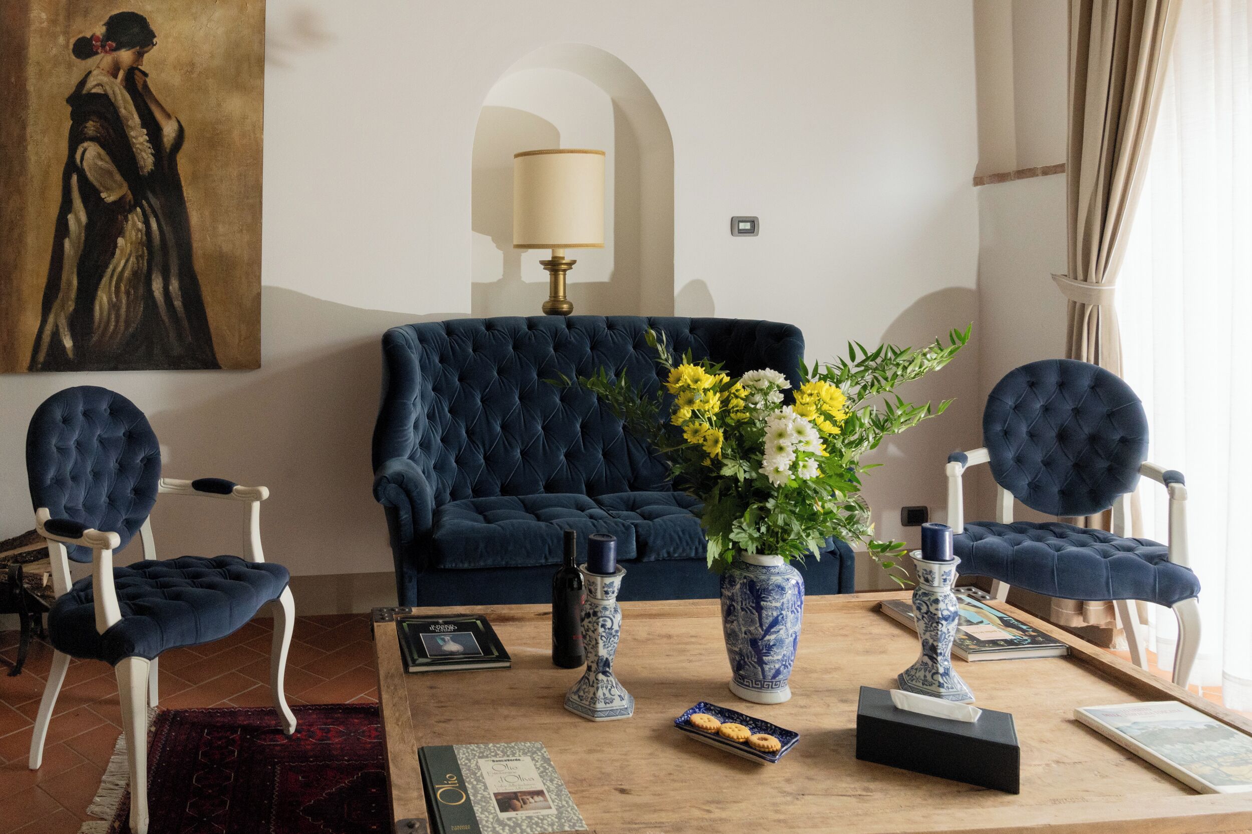 Uma sala de estar com um sofá azul escuro, duas poltronas estofadas em azul, uma mesa de centro de madeira e um vaso com flores.