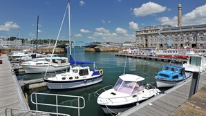 Uma marina com vários barcos atracados, um cais de madeira e um edifício grande ao fundo.