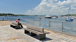 Um calçadão à beira-mar com bancos e grades, com vista para um porto cheio de barcos.