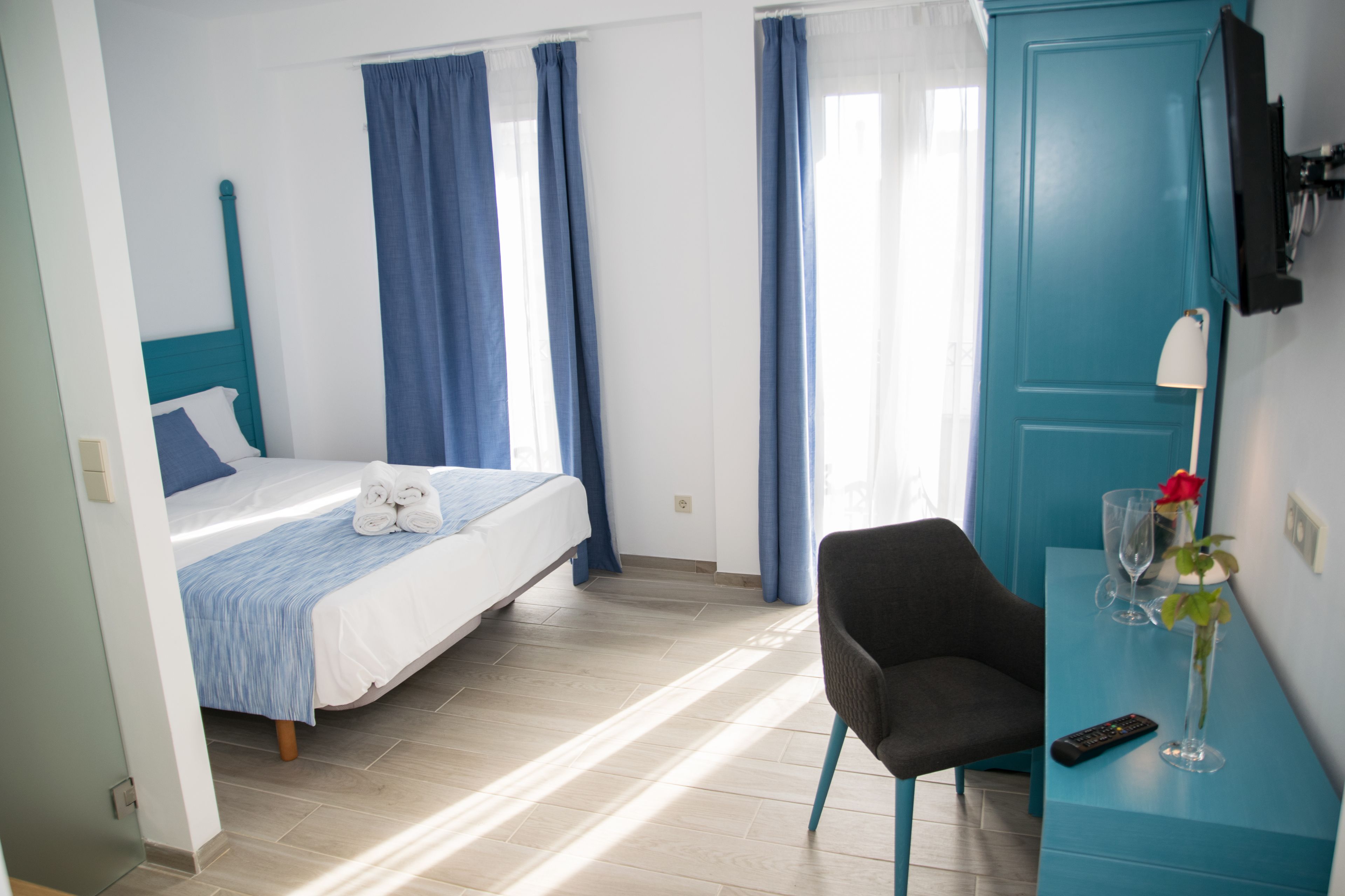 Um quarto com uma cama, uma cadeira, uma escrivaninha e uma televisão.